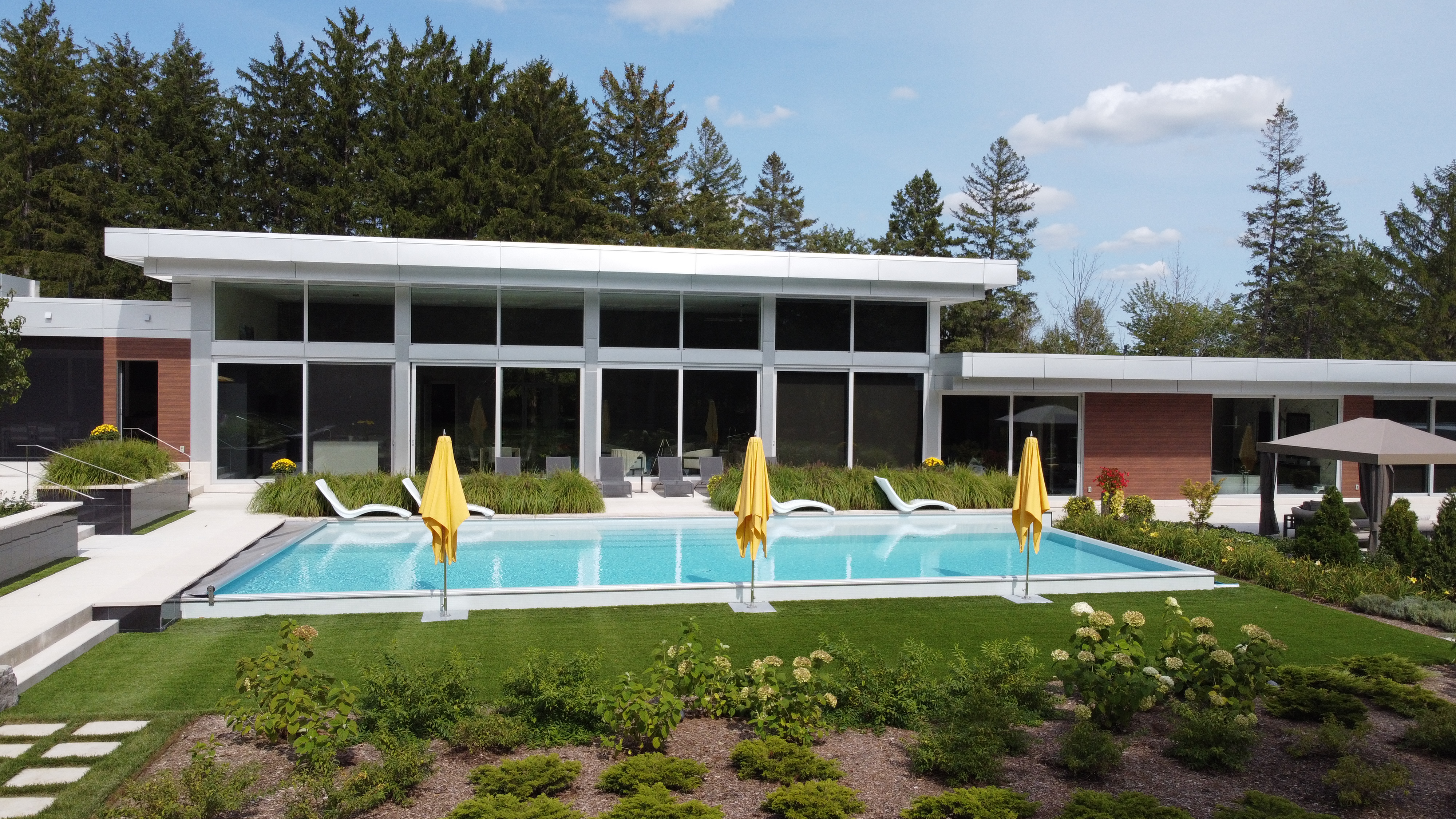 An outdoor residential pool with an infinity edge and yellow umbrellas ...