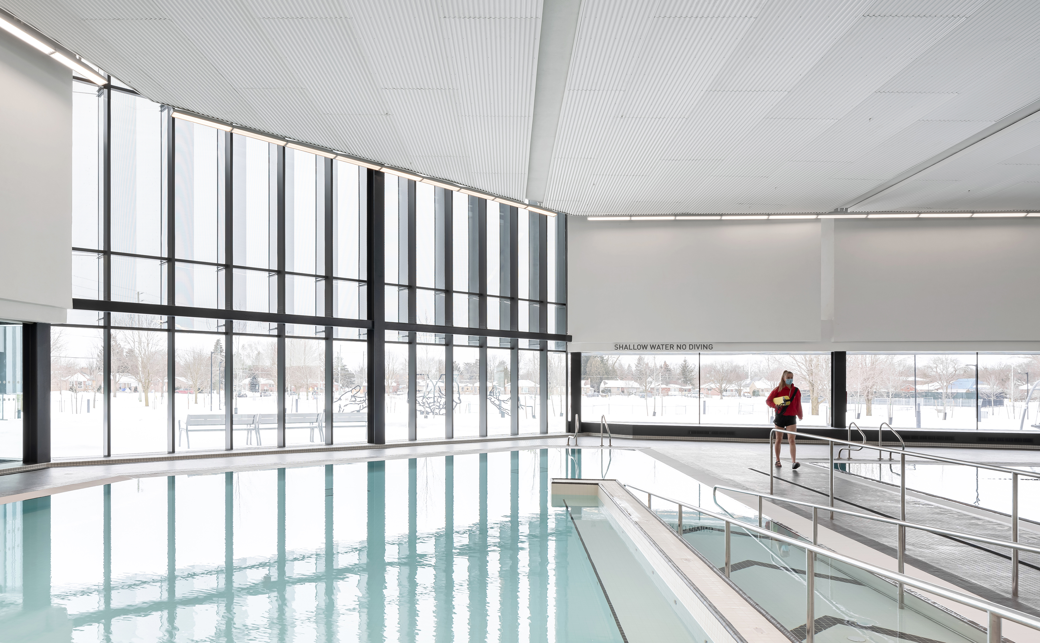 A modern indoor pool with high ceilings and large windows, letting in ...