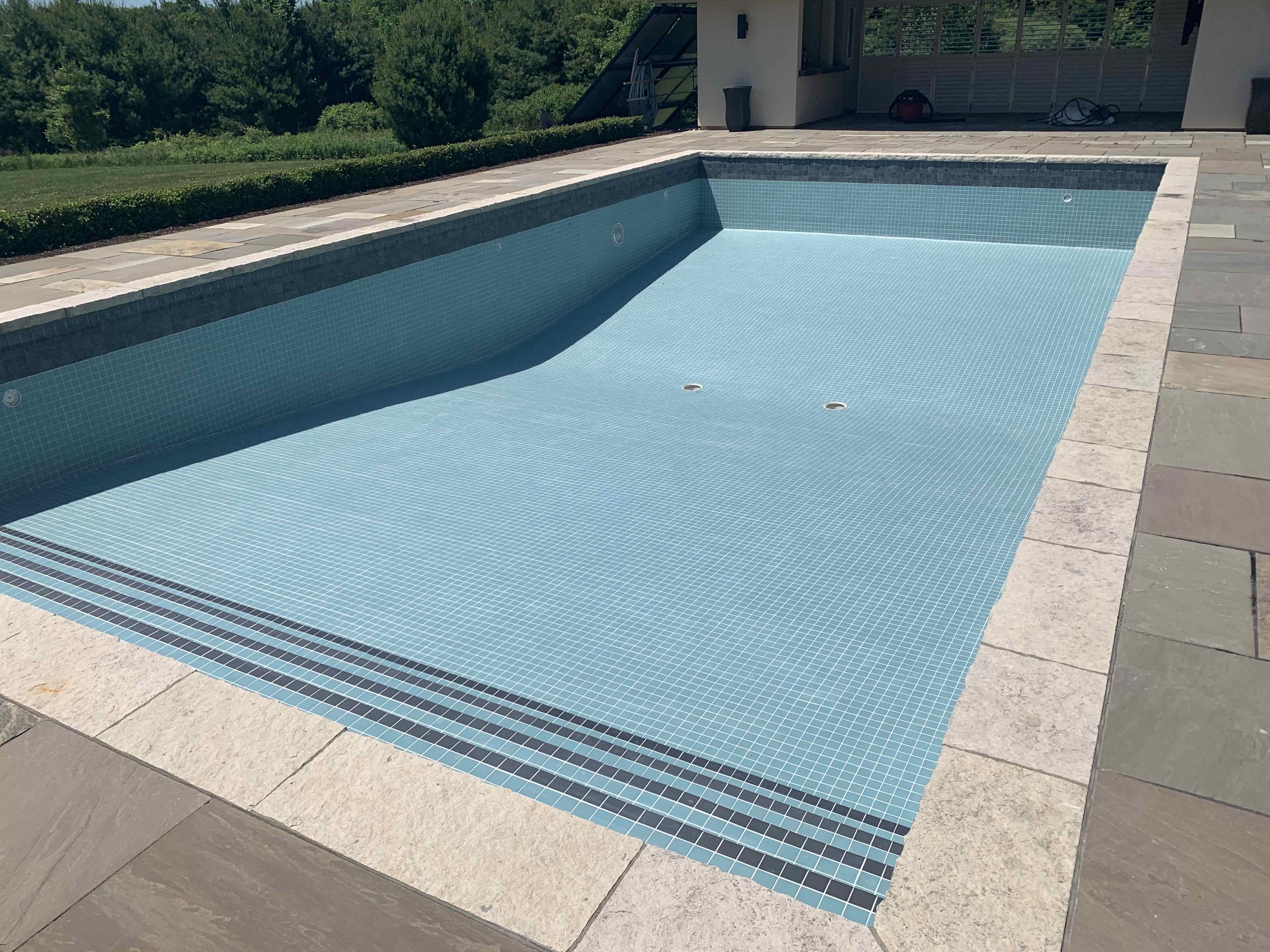 A rectangular pool with a light blue tile finish and dark blue ...