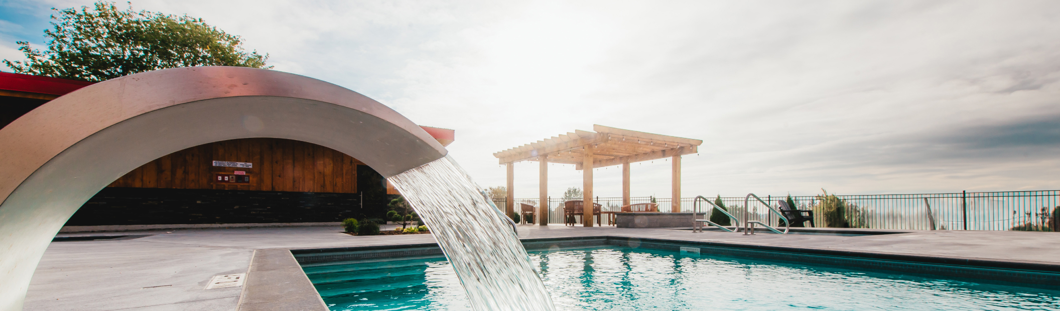 An outdoor pool with a curved water feature and a wooden pergola in the ...