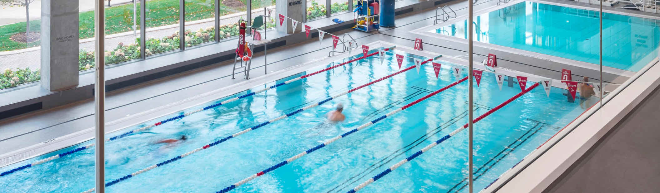 An indoor lap pool with swimmers, lifeguard chairs, and large windows ...