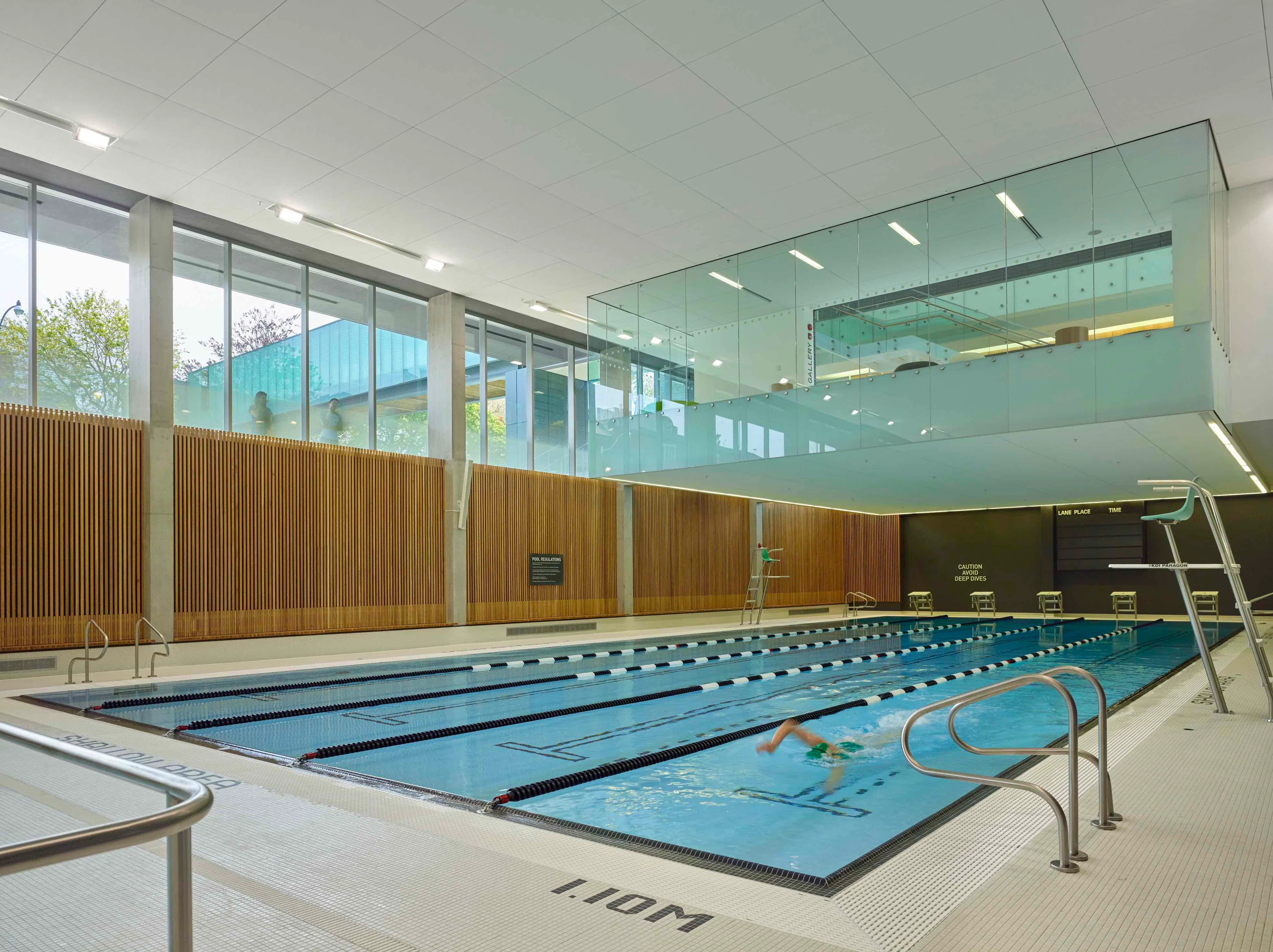 A modern indoor lap pool with a swimmer, wooden accent walls, and a ...
