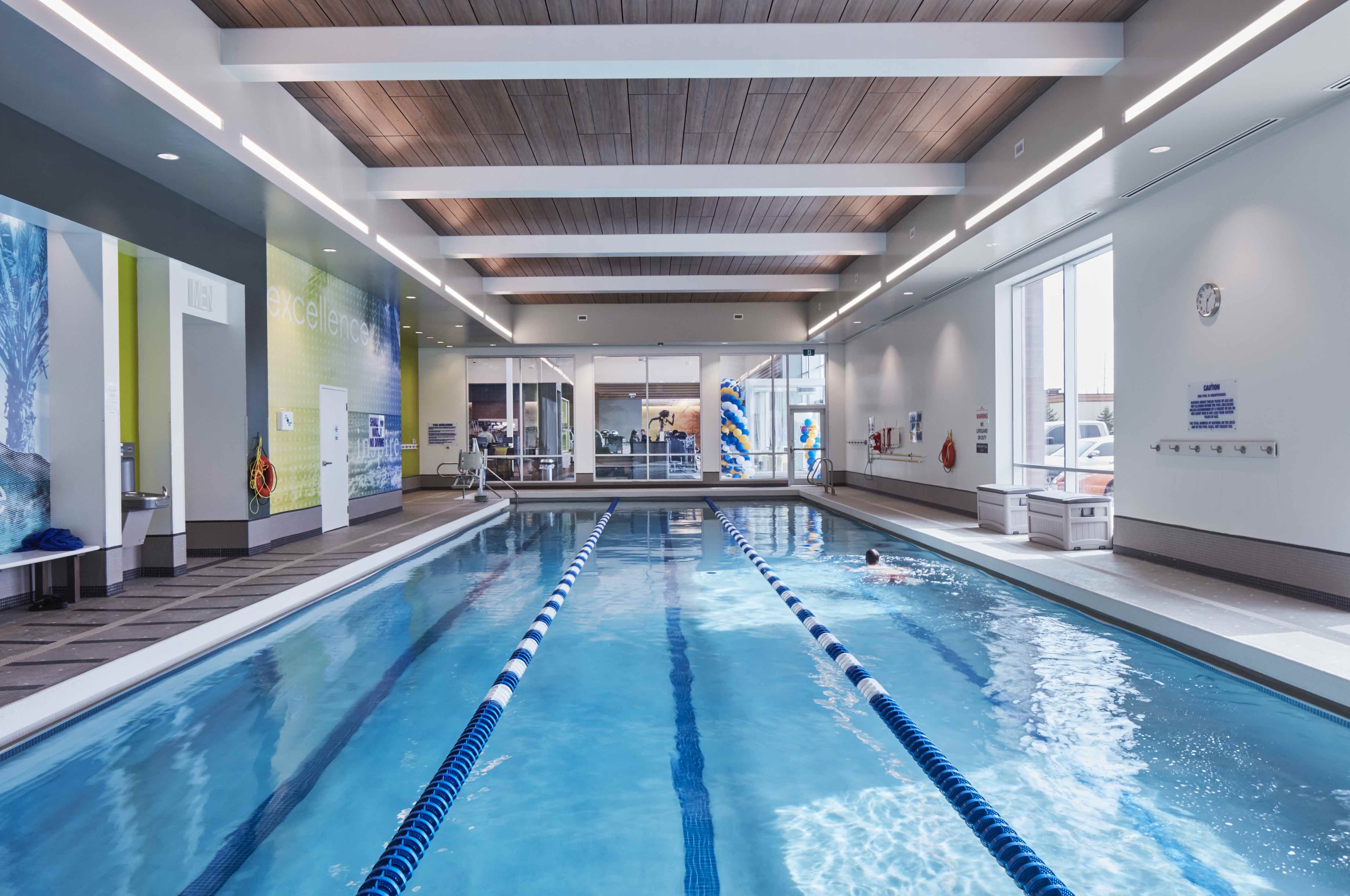 An indoor lap pool with blue lane dividers, wooden ceiling accents, and ...