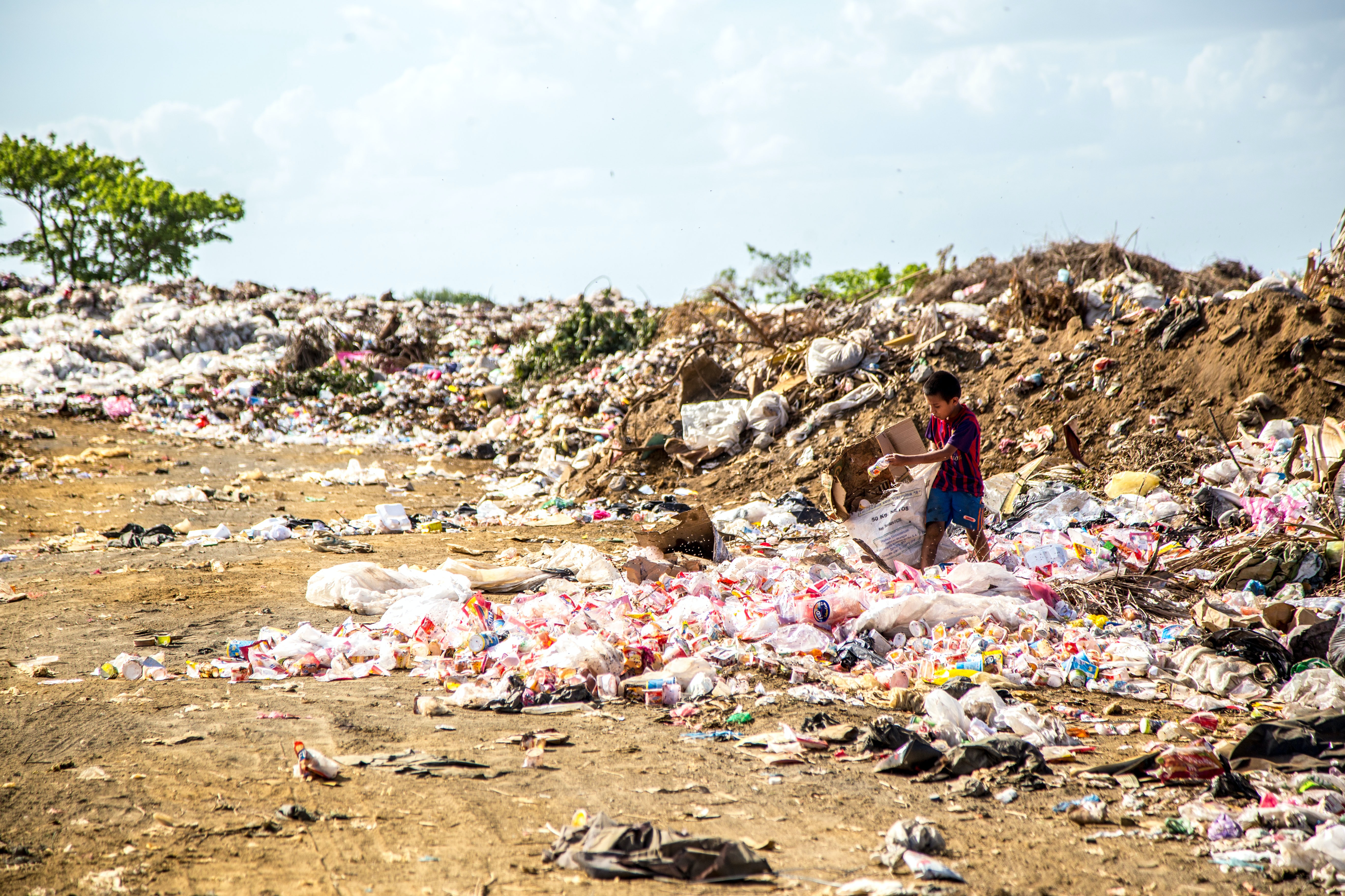 Boy working in a landfill surrounded by plastic.
