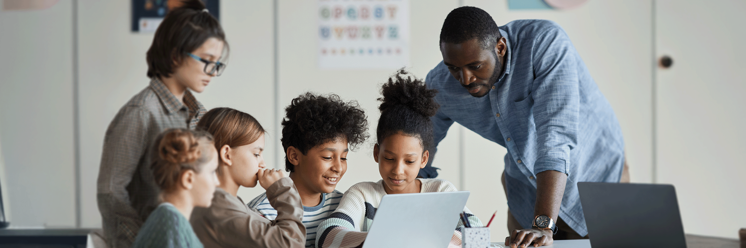 A teacher and kids collaborating on a laptop, sharing ideas